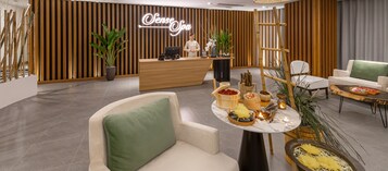 Uma área de recepção de spa moderna, com um balcão de madeira, um recepcionista e um espaço de estar com uma mesa posta para refeição.