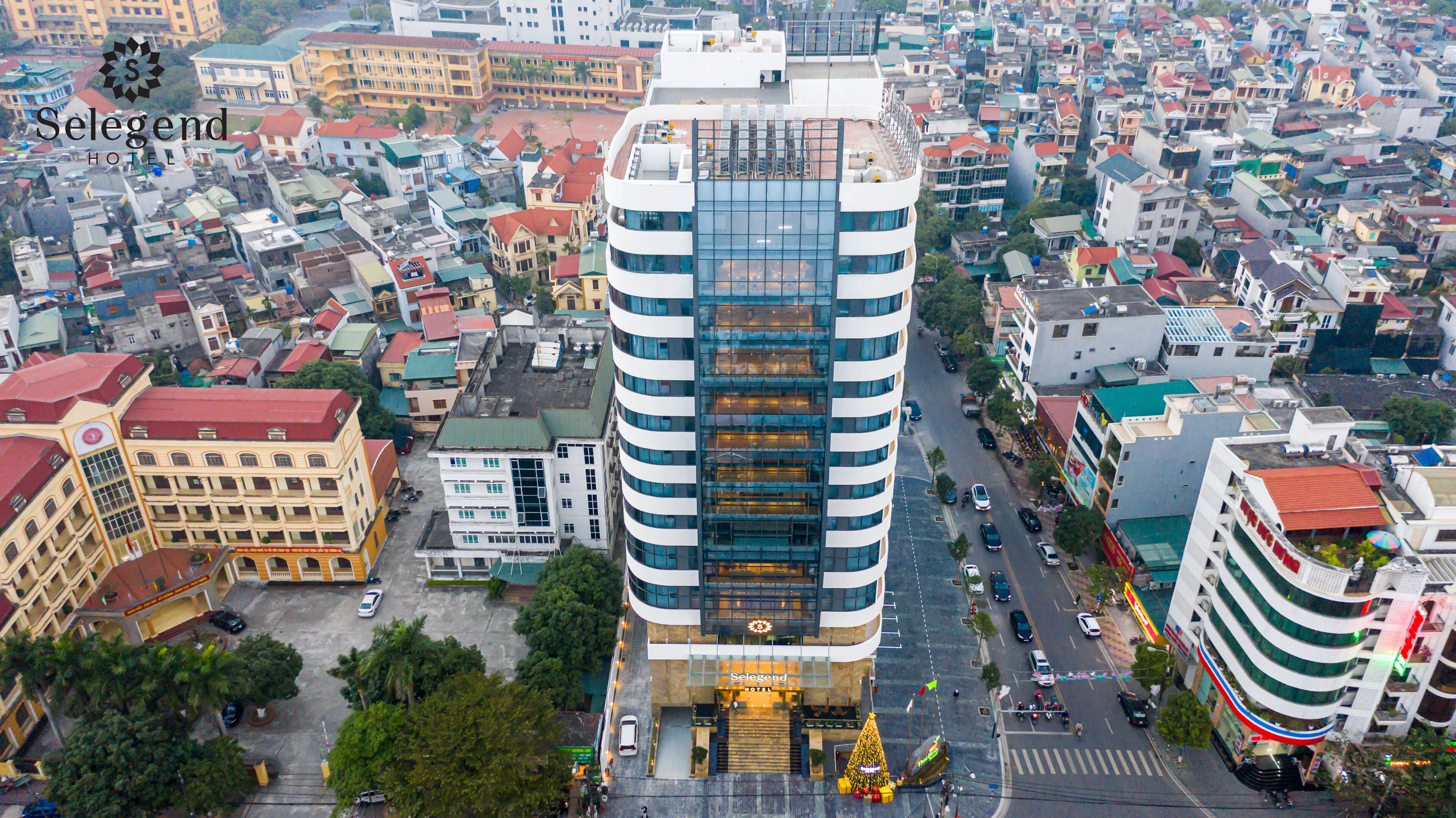 Um hotel moderno com fachada de vidro destacada, rodeado por uma área urbana densa com diversos edifícios.
