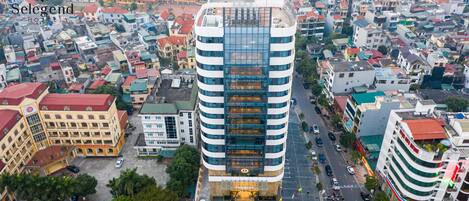 Um hotel moderno com fachada de vidro destacada, rodeado por uma área urbana densa com diversos edifícios.