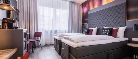 Quarto de hotel moderno com uma cama grande, uma escrivaninha com máquina de café, uma cadeira e uma televisão.
