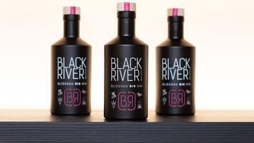 Três garrafas de Gin Black River Bliesgauw Bio dispostas sobre uma superfície de madeira.