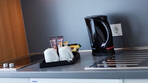 Uma estação de café com uma cafeteira preta, chávenas brancas e cápsulas de café sobre um balcão.