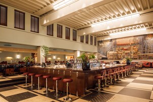 Um hall amplo com um balcão de bar extenso, diversas áreas de estar e um grande mural na parede.