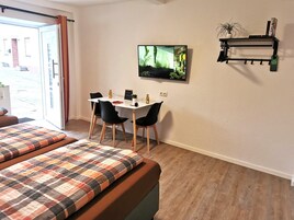 Um quarto com cama, uma mesa e cadeiras, televisão e uma estante com livros e uma planta.