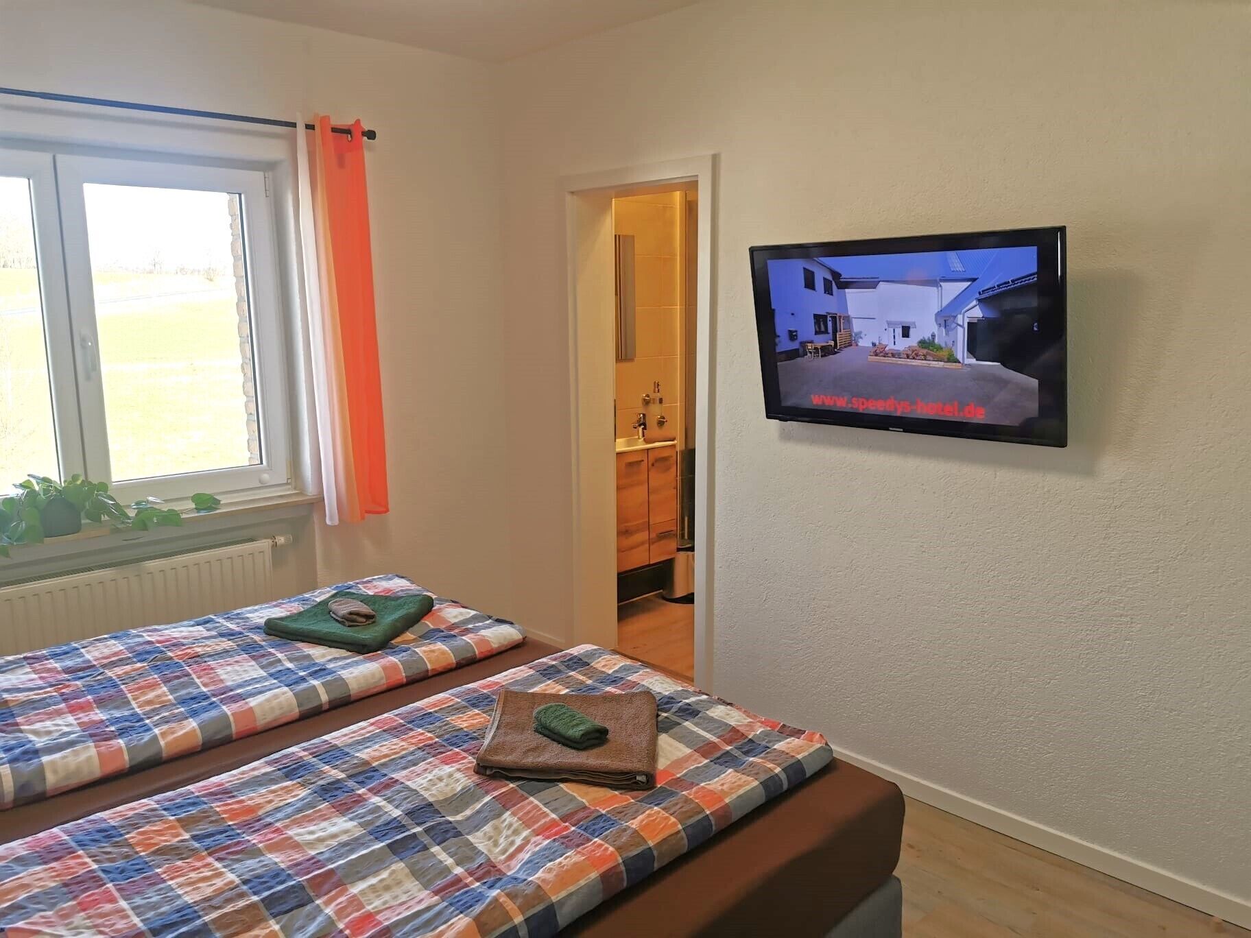 Quarto de hotel com duas camas, uma televisão na parede e vista para o exterior.
