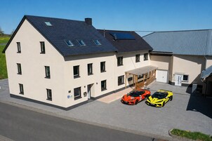 Um edifício moderno de dois andares com garagem, dois carros esportivos e um painel solar no telhado.