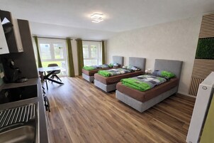 Quarto moderno com três camas, um espaço de cozinha compacta e uma área de refeições.