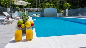 Piscina com espreguiçadeiras e guarda-sóis, cercada por vegetação.