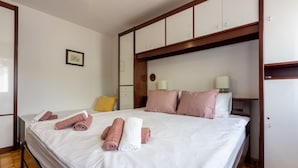 Uma cama bem arrumada com toalhas enroladas, uma mesa de cabeceira com abajur e um guarda-roupa em um quarto de hotel.