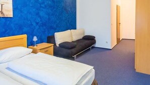 Quarto de hotel com cama, mesa de cabeceira, sofá e parede azul com textura.