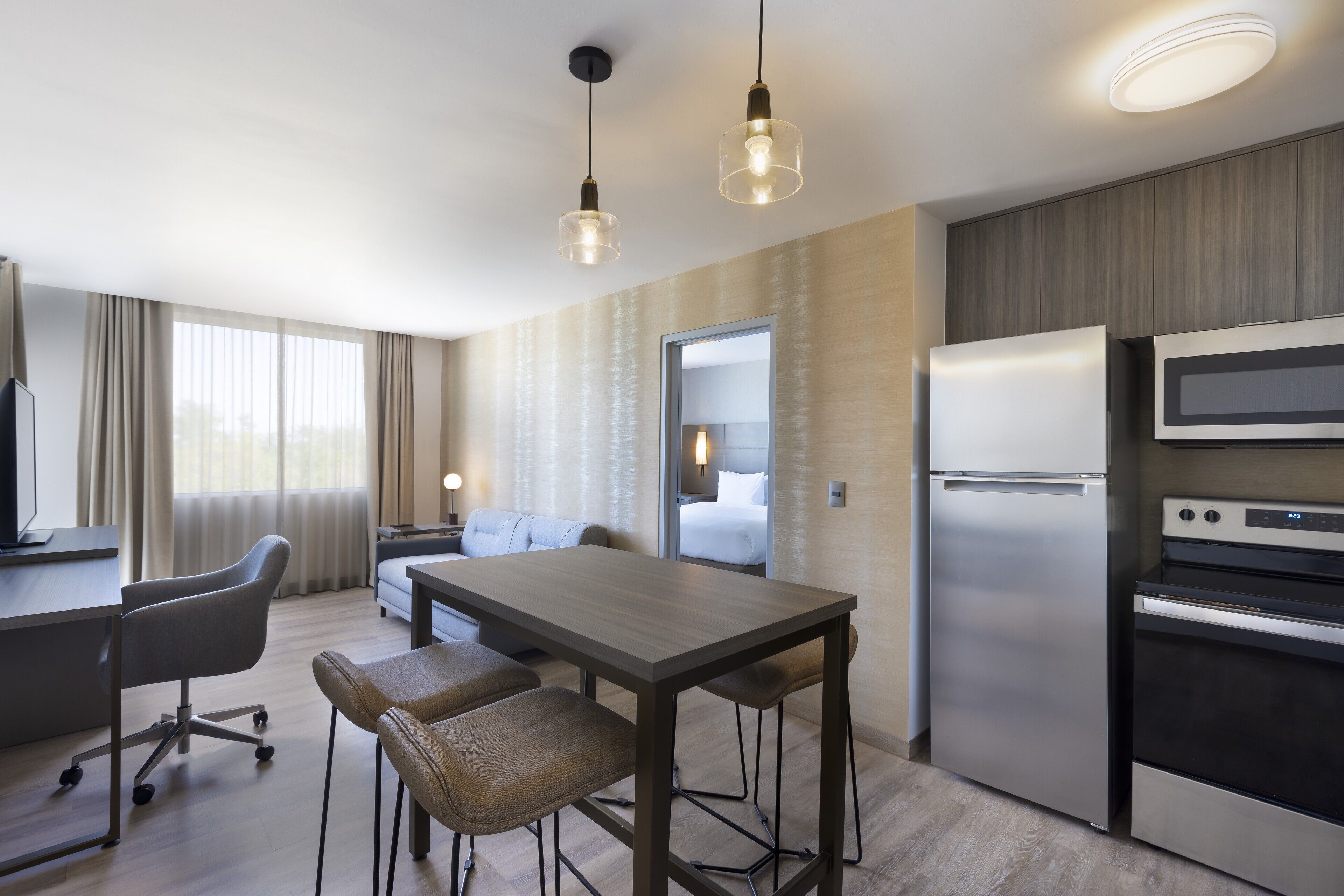 Quarto de hotel moderno com mesa de jantar de madeira, duas cadeiras, um sofá, uma TV, um frigorífico e um micro-ondas.