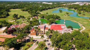 Vista aérea de um campo de golfe com um clube, várias lagoas e vegetação ao redor.