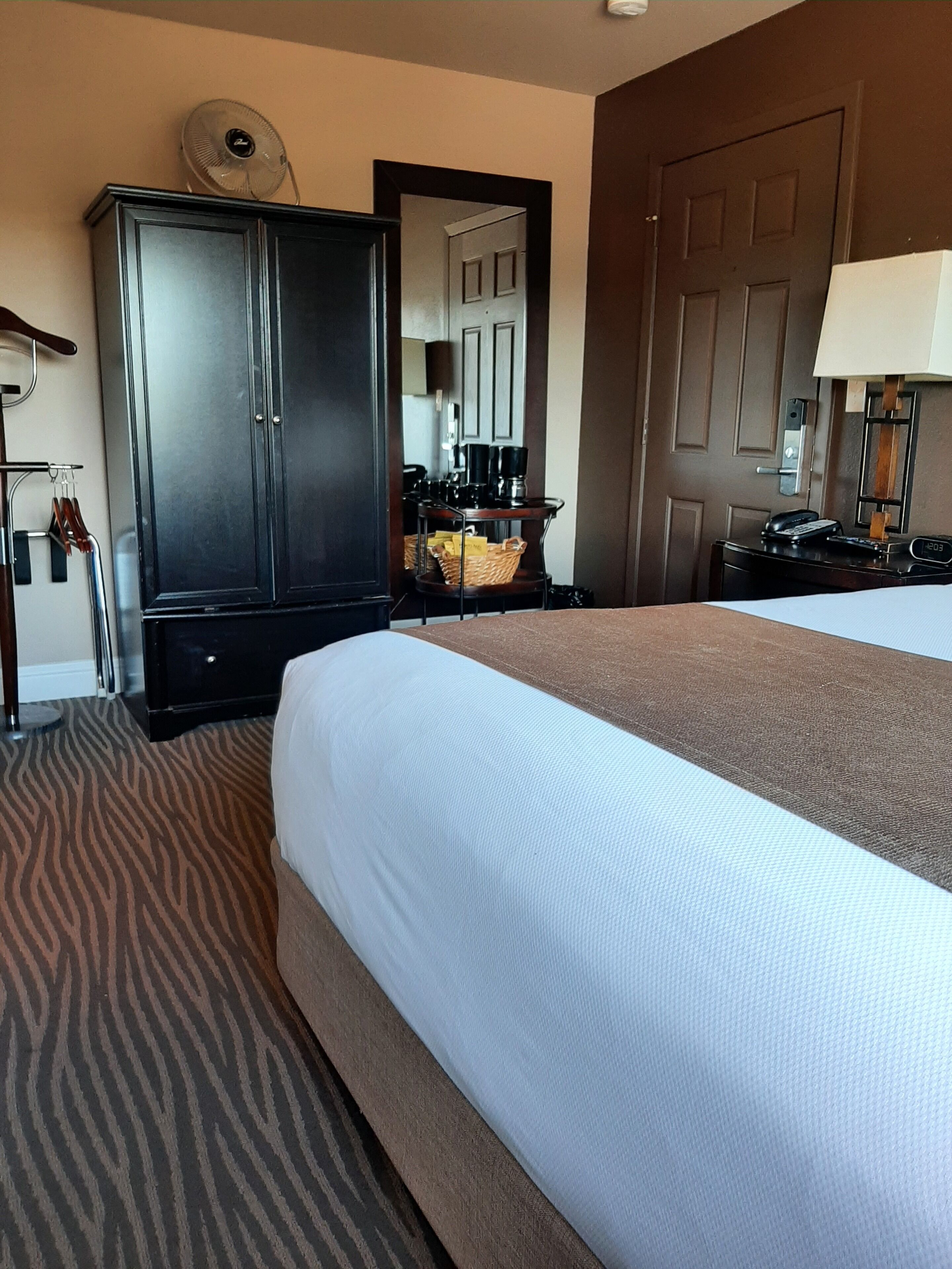 Quarto de hotel com cama grande, guarda-roupa, secretária com luminária e máquina de café.
