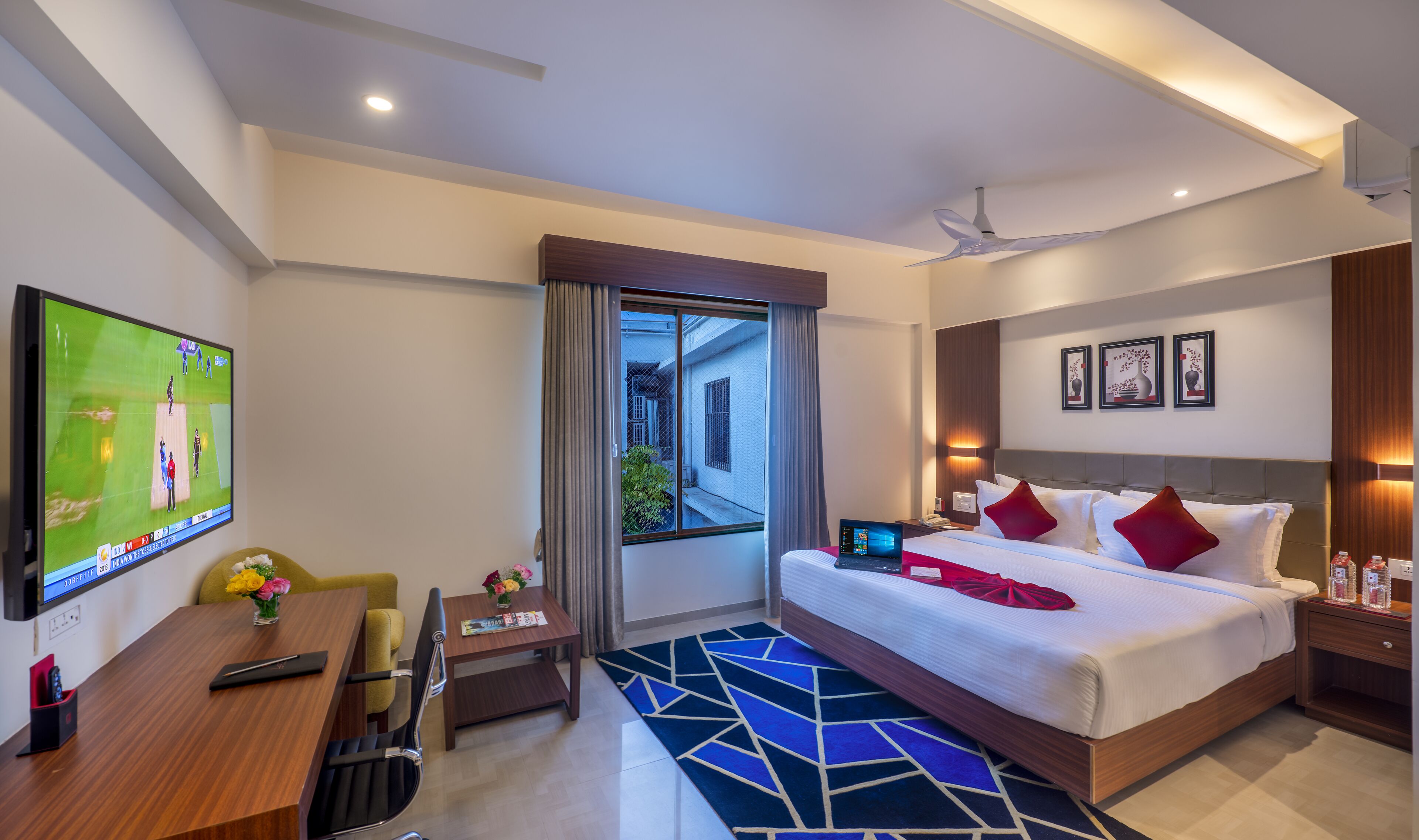 Quarto de hotel com cama, escrivaninha com televisão, janela e vista para o exterior.