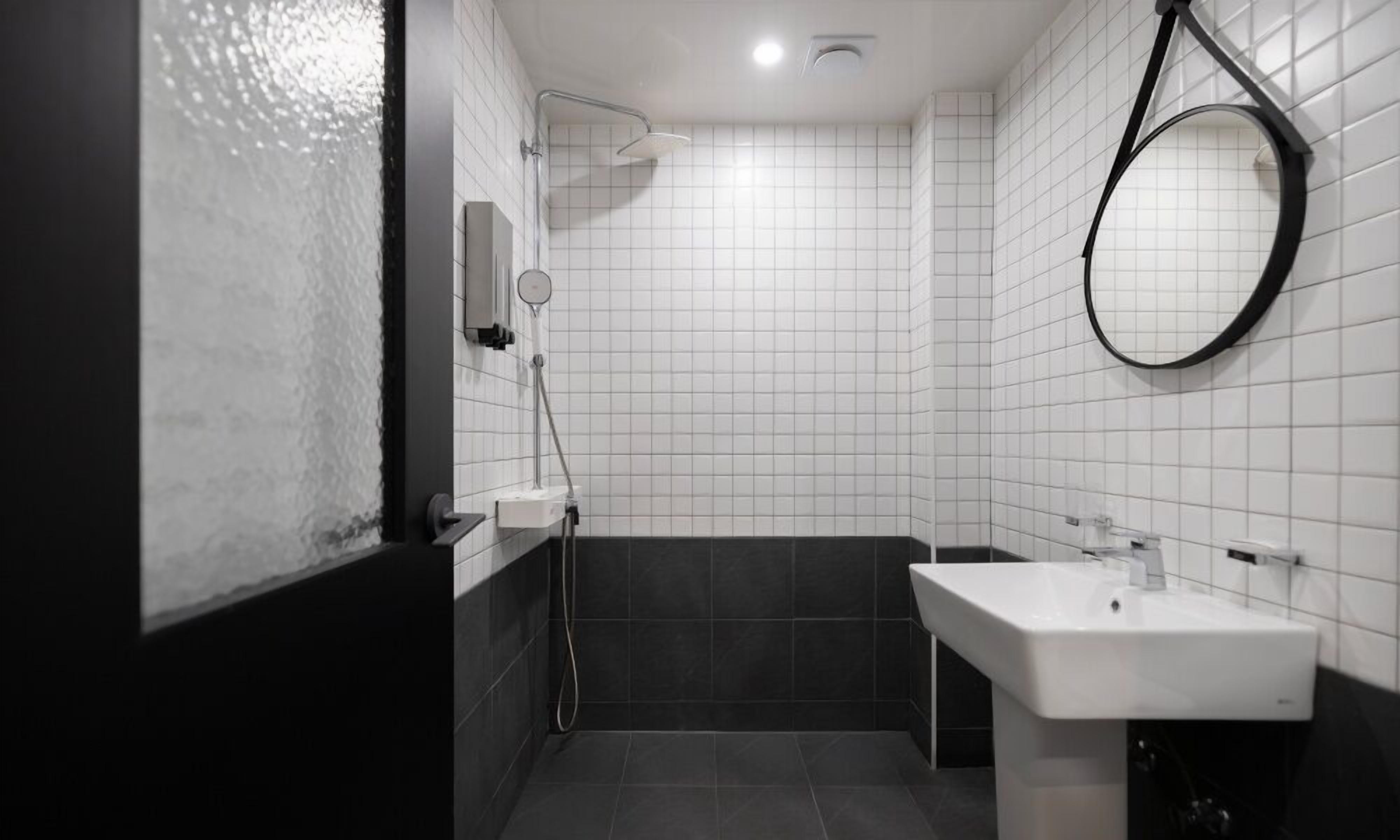 Um banheiro moderno com paredes revestidas de azulejos brancos, uma banheira preta e uma pia branca.