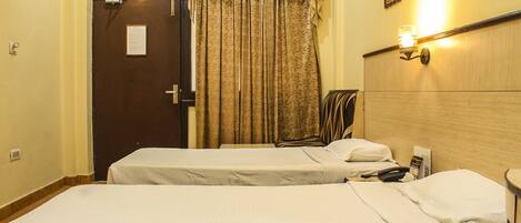 Quarto de hotel com duas camas, uma porta, uma cortina, uma luminária na parede e uma mesa de cabeceira com telefone.
