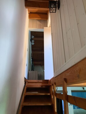 Escada de madeira que leva a um quarto com teto branco e um painel decorativo na parede.