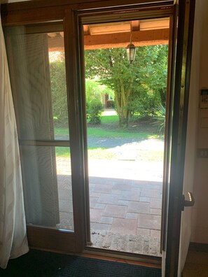 Porta de vidro que dá para uma área externa pavimentada, com uma árvore e um caminho.