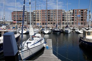 Marina com vários barcos atracados, um cais de madeira e um edifício com vários andares ao fundo.