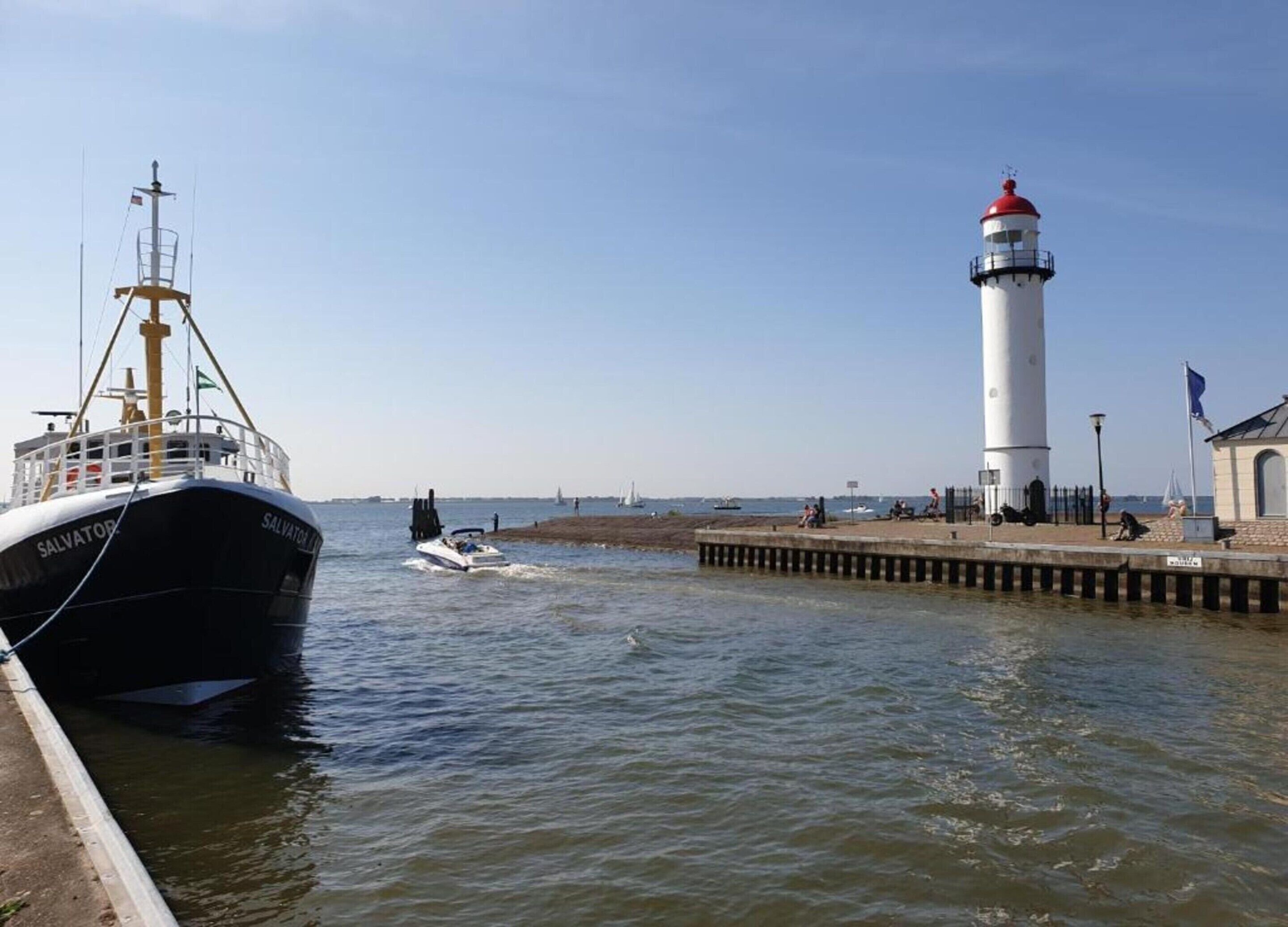 Um barco chamado 'SALVATOR' atracado em um cais, com um farol ao fundo.