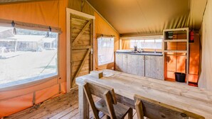 Um quarto com tenda, uma mesa de madeira, cadeiras, pia e janela.