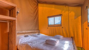Uma cama de solteiro com lençóis e almofadas brancos, cabeceira de madeira e uma janela com cortinas.