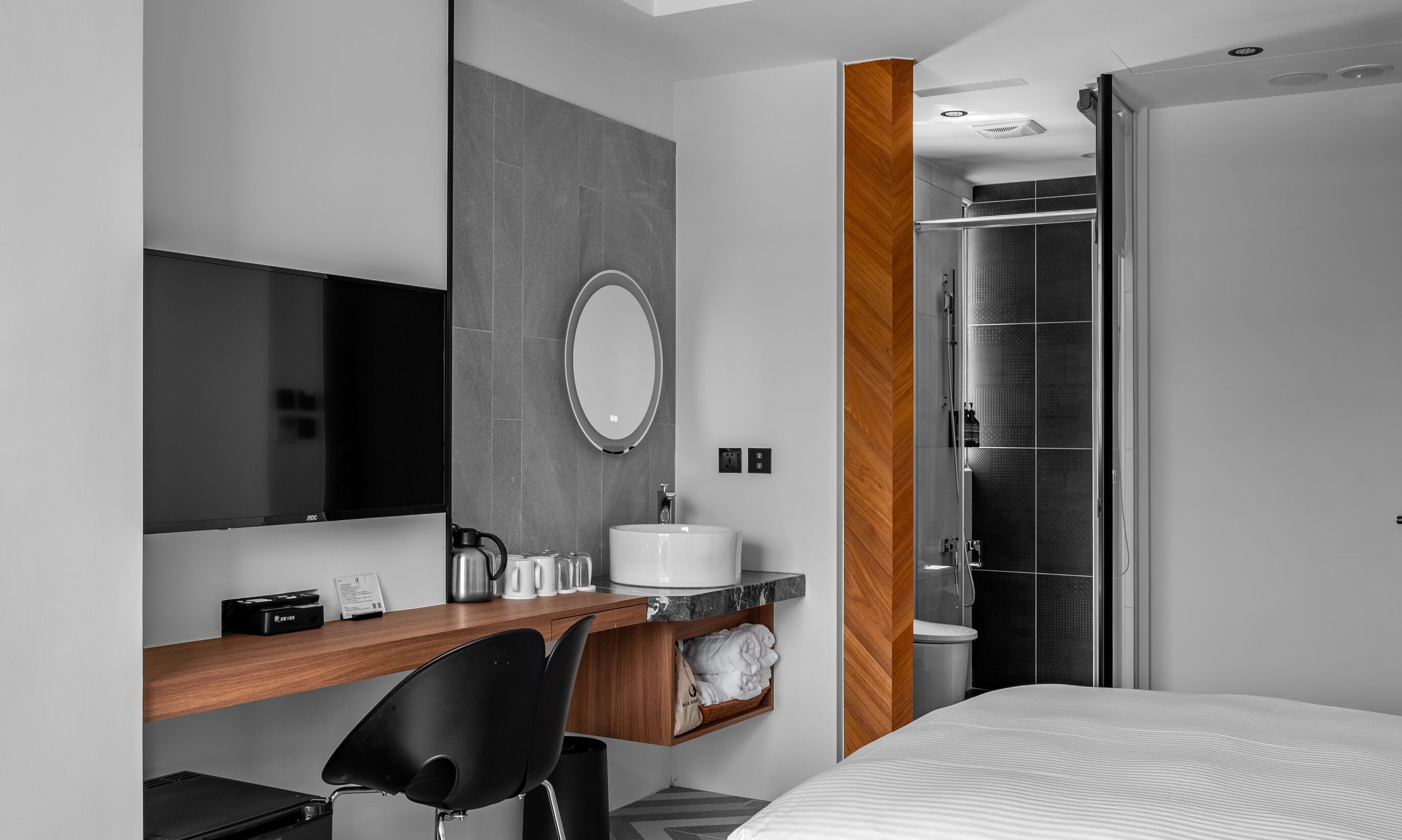 Quarto de hotel moderno com uma cama grande, uma escrivaninha de madeira com uma cadeira, televisão de tela plana, pia embutida e área de chuveiro.