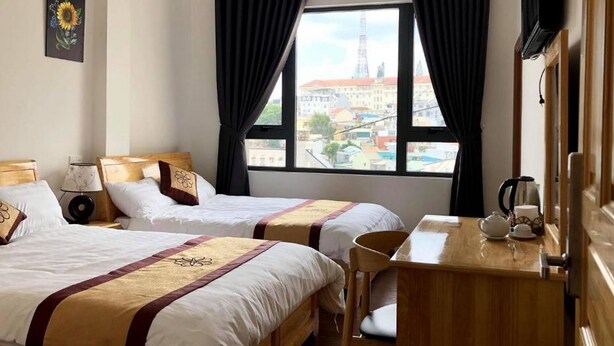 Quarto de hotel com duas camas, uma escrivaninha de madeira, uma cadeira, janela com cortinas e vista para a cidade.