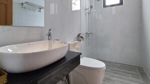 Uma casa de banho com uma grande pia oval, uma sanita e um chuveiro.