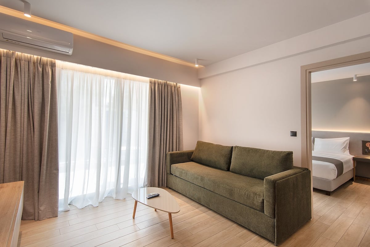 Quarto de hotel moderno com um sofá verde, uma mesinha e uma cama com criado-mudo.