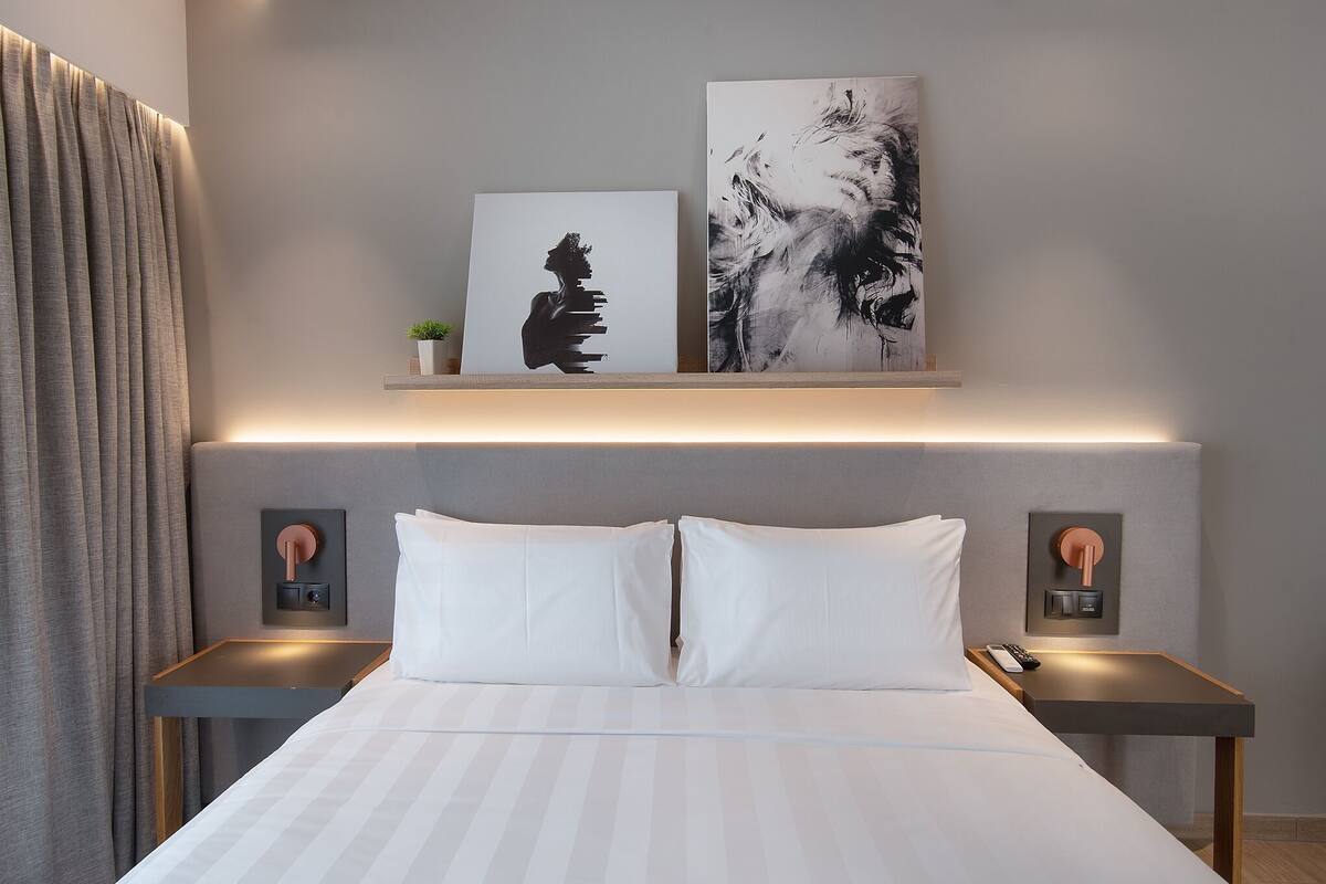 Quarto de hotel moderno com cama grande, duas mesinhas de cabeceira e obras de arte na parede.