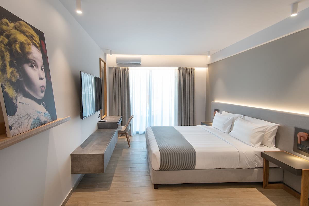 Quarto de hotel moderno com uma cama grande, uma escrivaninha, uma cadeira e uma televisão.