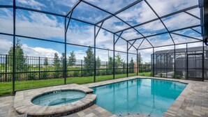 Piscina coberta ao ar livre com hidromassagem, cercada por uma grade de metal e vista para uma área gramada.