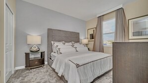 Quarto com cama, mesas de cabeceira, cômoda e janela com cortinas.