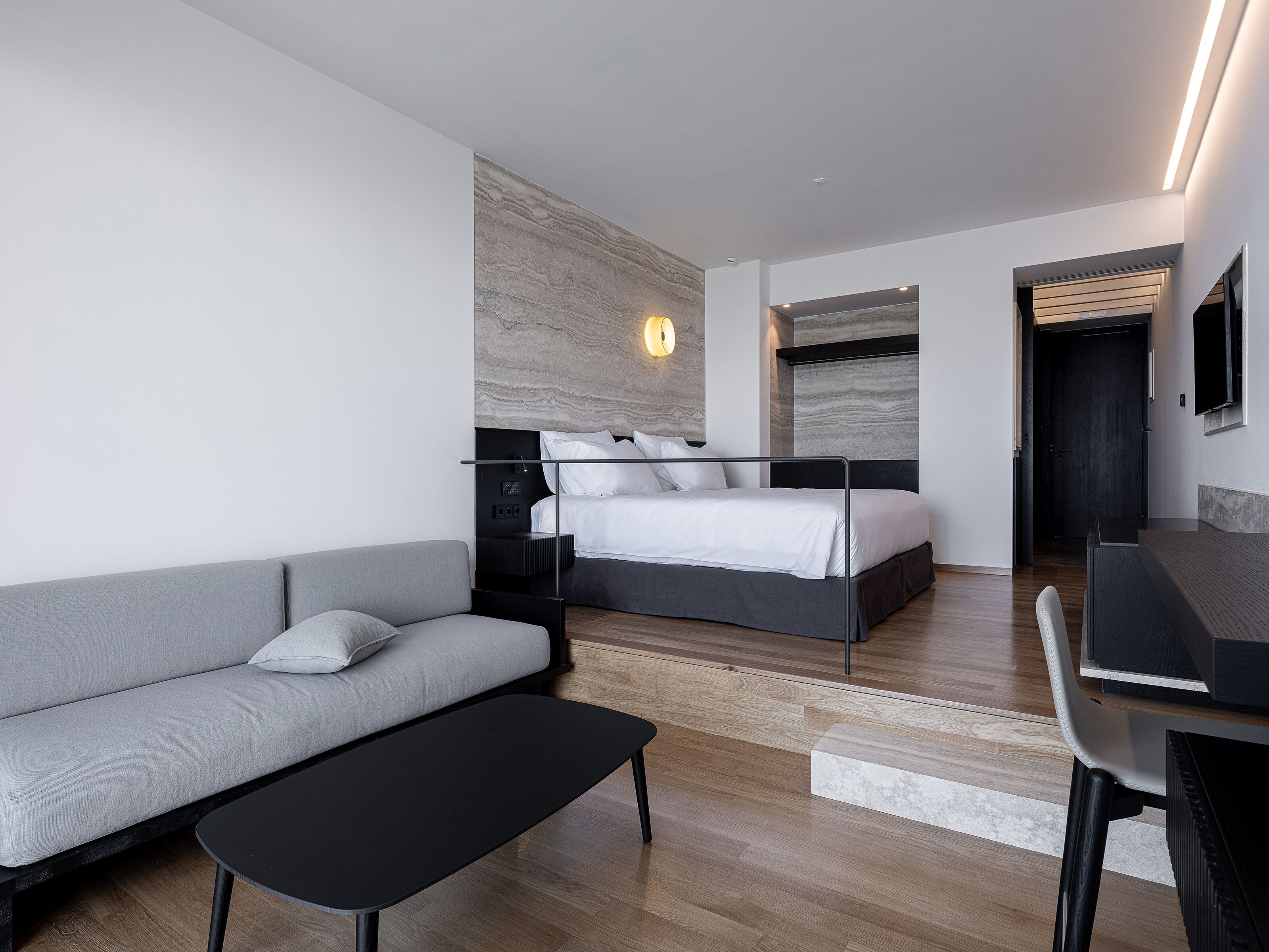 Quarto de hotel moderno com cama, sofá, escrivaninha e uma mesinha.