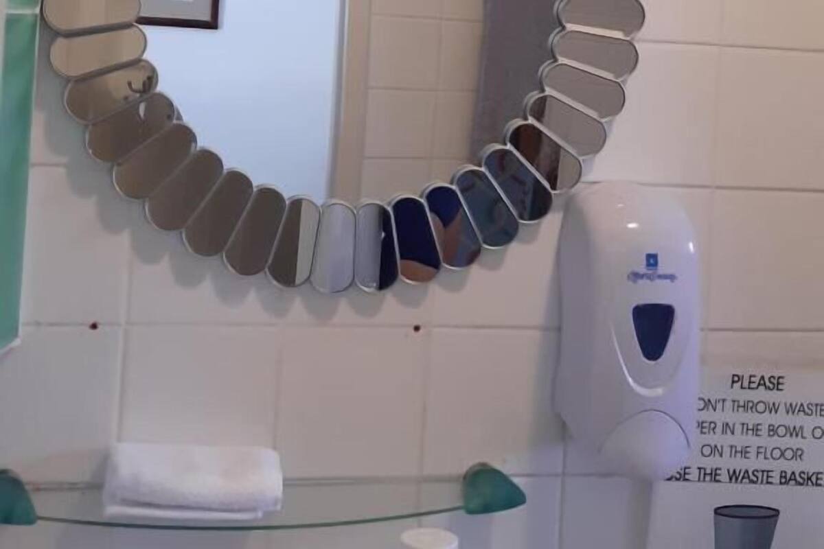 Casa de banho com espelho redondo, dispensador de sabonete e suporte para toalhas.