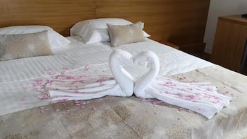 Cama arrumada com arranjo de toalha em formato de coração e pétalas de rosa espalhadas.