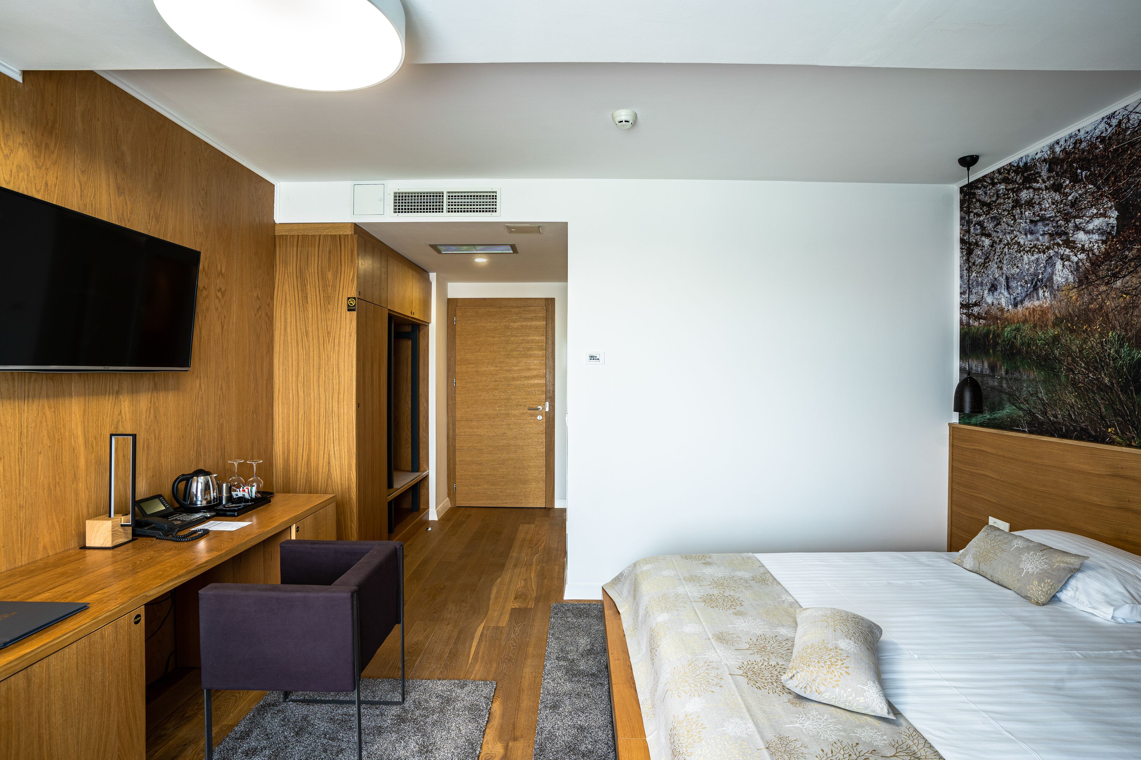 Quarto de hotel moderno com uma cama grande, uma escrivaninha com cadeira, televisão de tela plana e um quadro na parede.