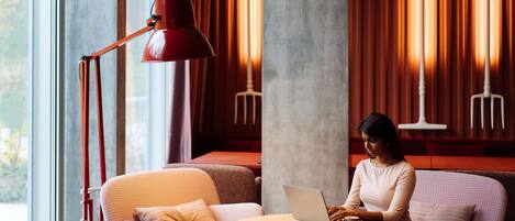 Uma mulher usando um laptop em uma mesa redonda em um interior moderno com móveis estampados e um abajur vermelho.