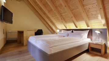 Quarto com teto inclinado, cama com roupa de cama branca, abajur e televisão de tela plana na parede.