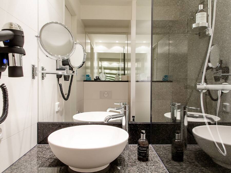Uma casa de banho moderna com uma grande pia branca, dois espelhos, um secador de cabelo e uma área de duche.