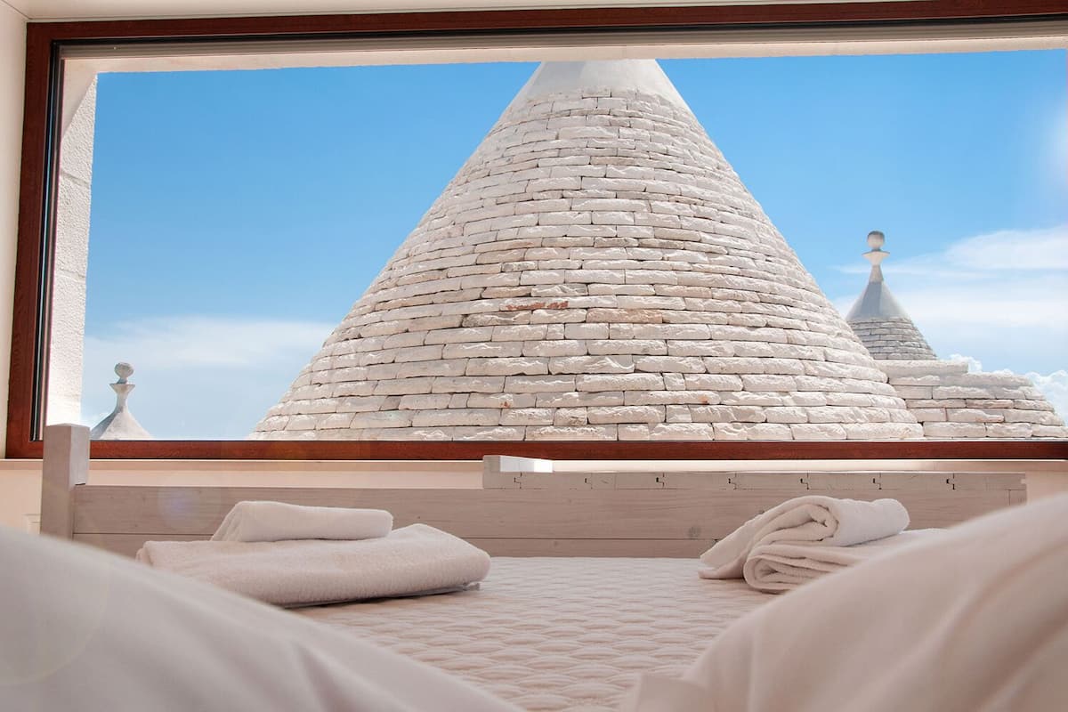 Quarto de hotel com uma janela grande que dá para uma construção de pedra.