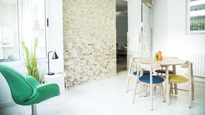 Quarto moderno com parede de pedra, mesa redonda com cadeiras, uma cadeira verde e uma mesinha de cabeceira com abajur.