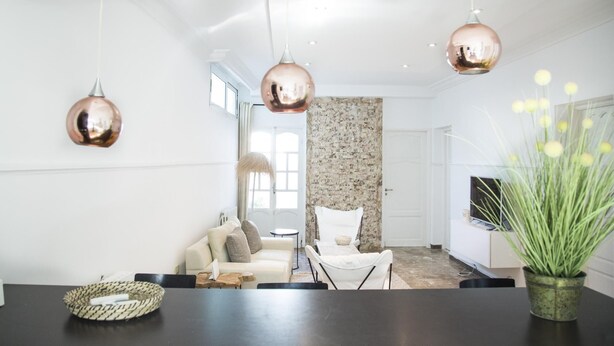 Uma sala de estar moderna com sofá, mesa de centro e área de jantar. Três luminárias pendentes no teto.