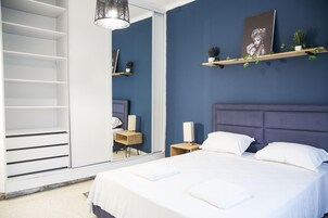 Quarto com cama, mesas de cabeceira, espelho e prateleira com objetos decorativos.