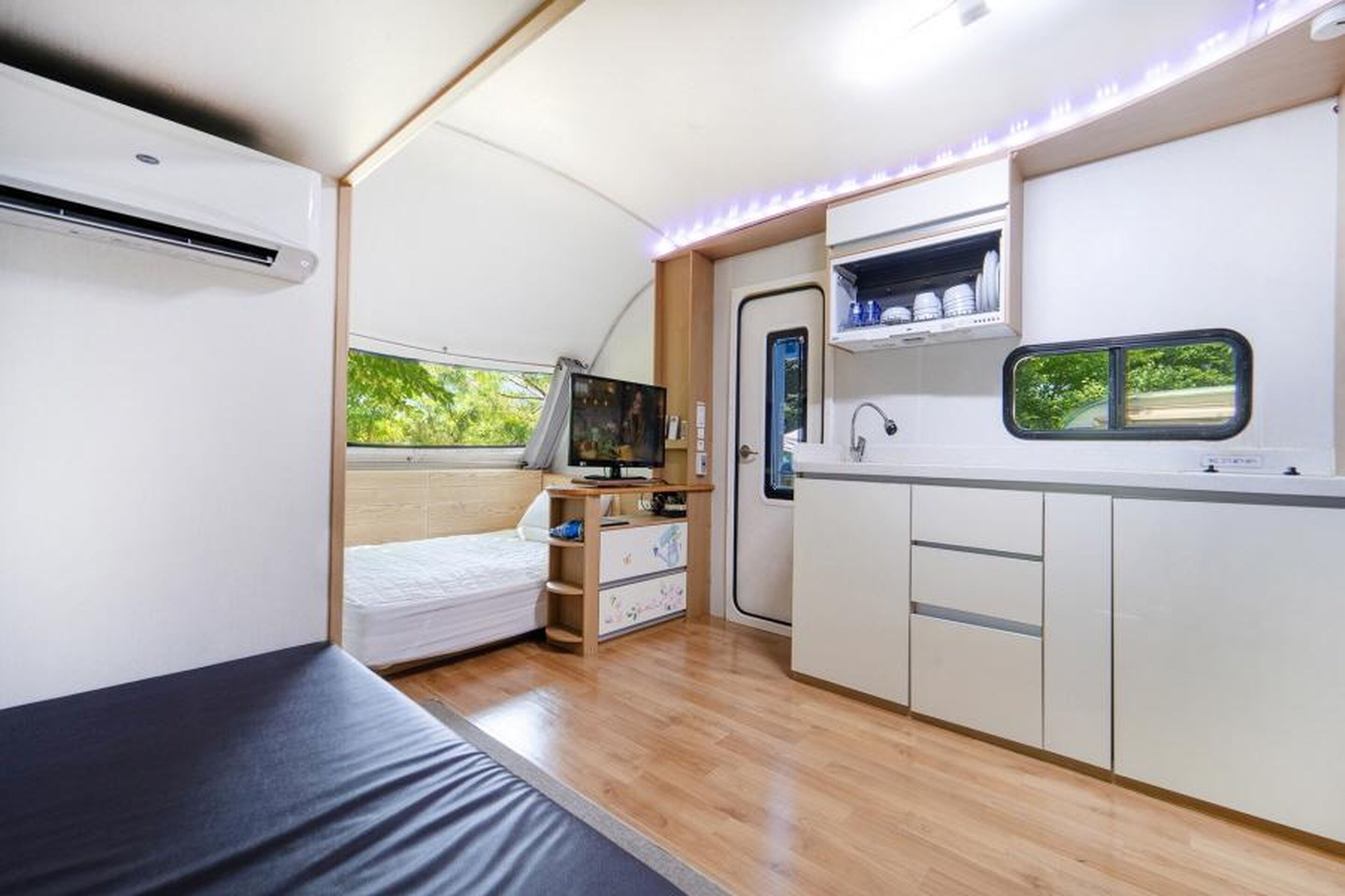 Interior compacto de uma van, com cama, pequeno espaço de cozinha e uma janela.