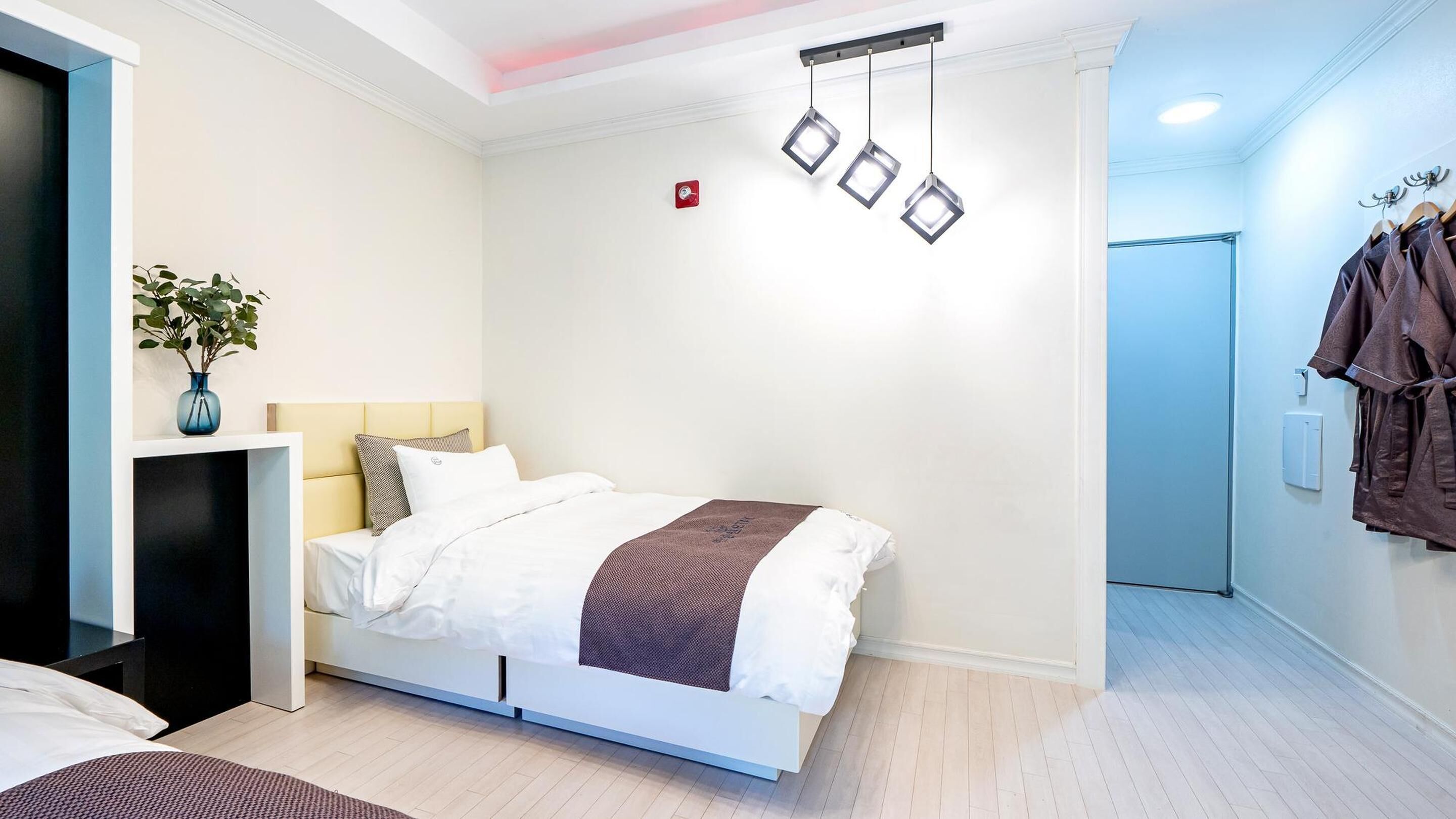 Quarto moderno com cama, mesa de cabeceira e luminária suspensa.
