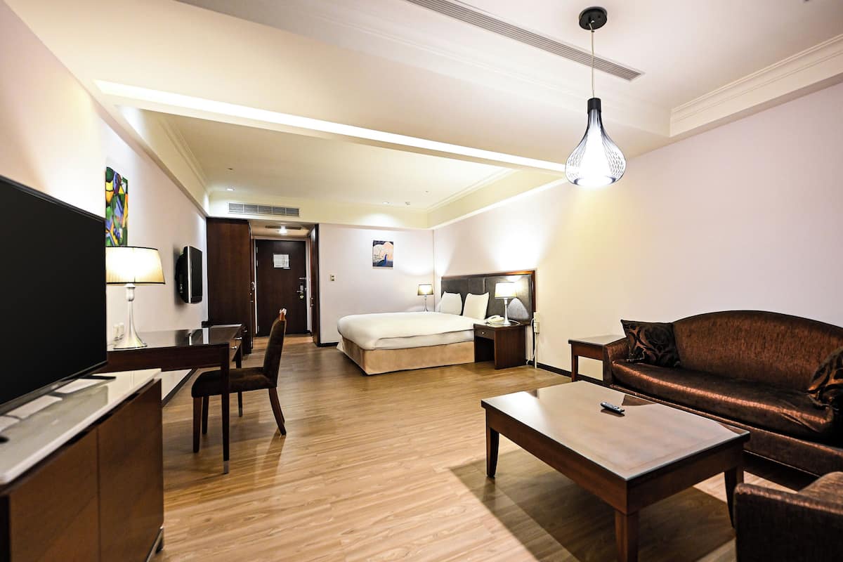 Quarto de hotel com cama, escrivaninha, cadeira, sofá e televisão.