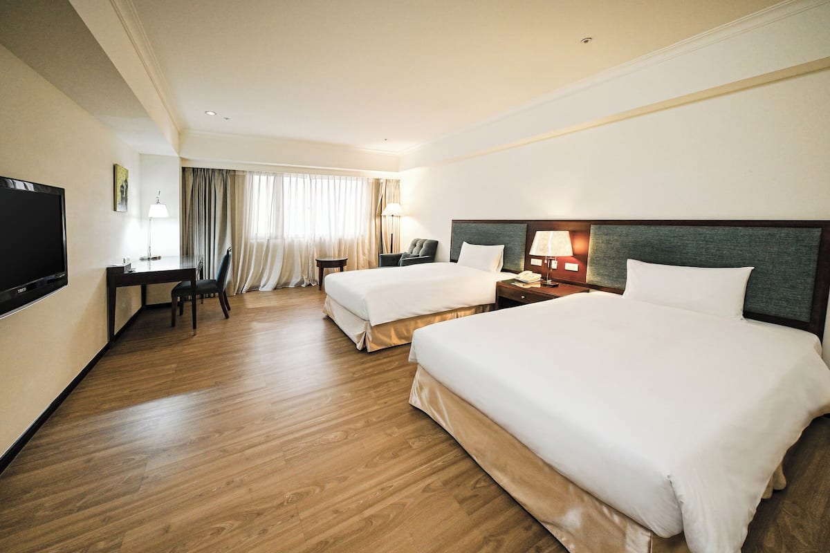 Quarto de hotel com duas camas, uma escrivaninha, uma televisão e uma janela com cortinas.
