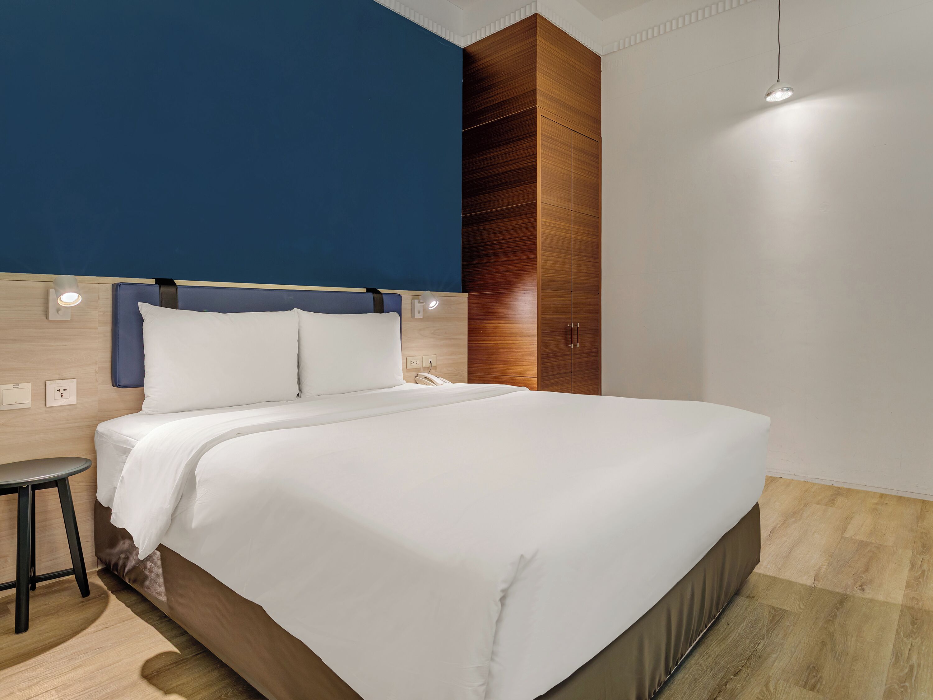 Quarto de hotel moderno com uma cama grande, mesa de cabeceira e um guarda-roupa.